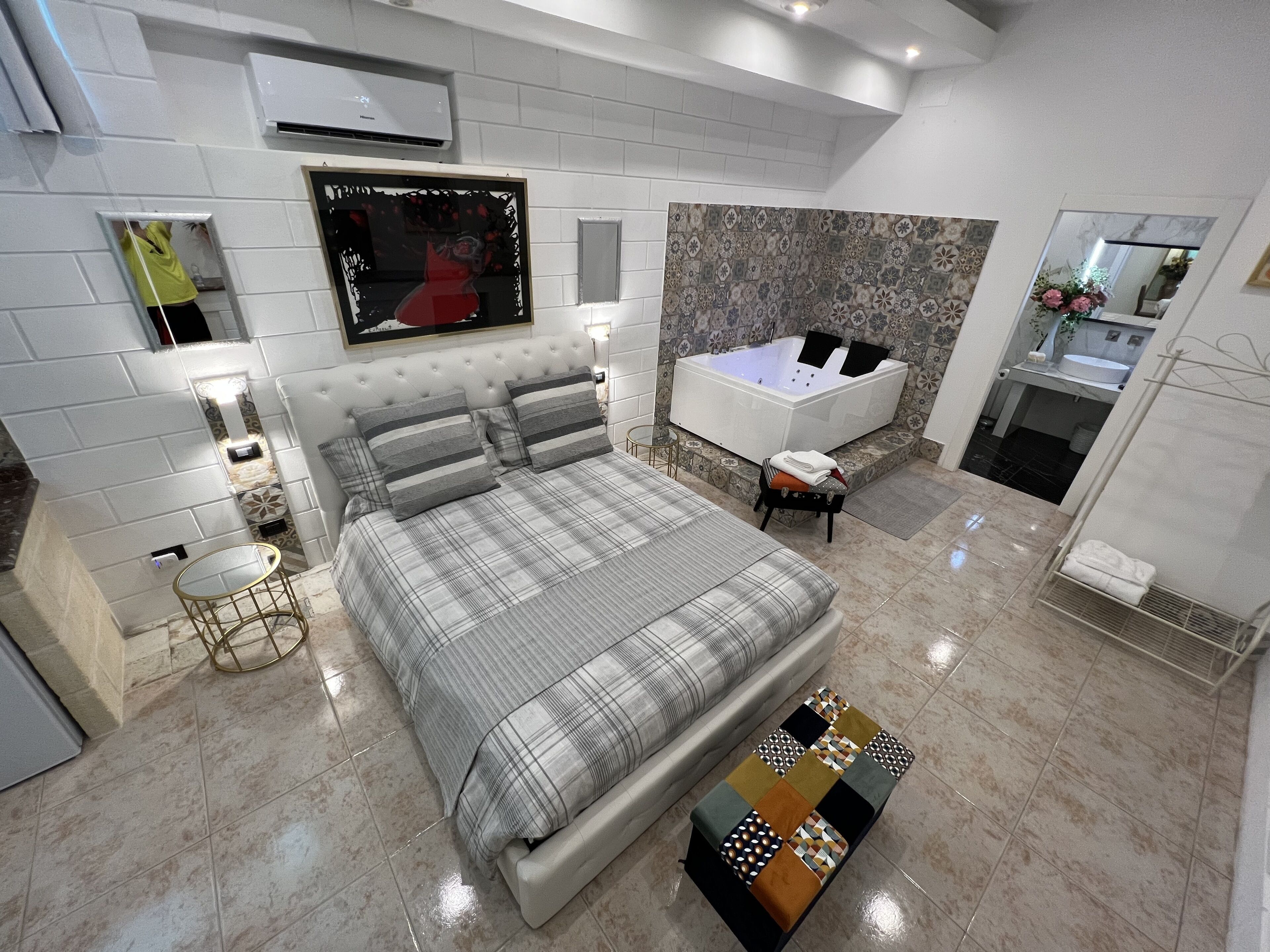 Quarto moderno com cama grande, área de estar, banheira e banheiro com pia e espelho.