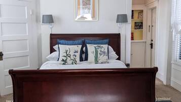 Quarto com uma grande cama de madeira, um ventilador de teto e um quadro na parede.