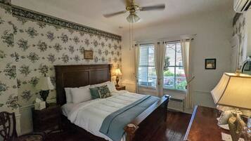 Quarto com cama de madeira, papel de parede floral, ventoinha no teto e janela com persianas.