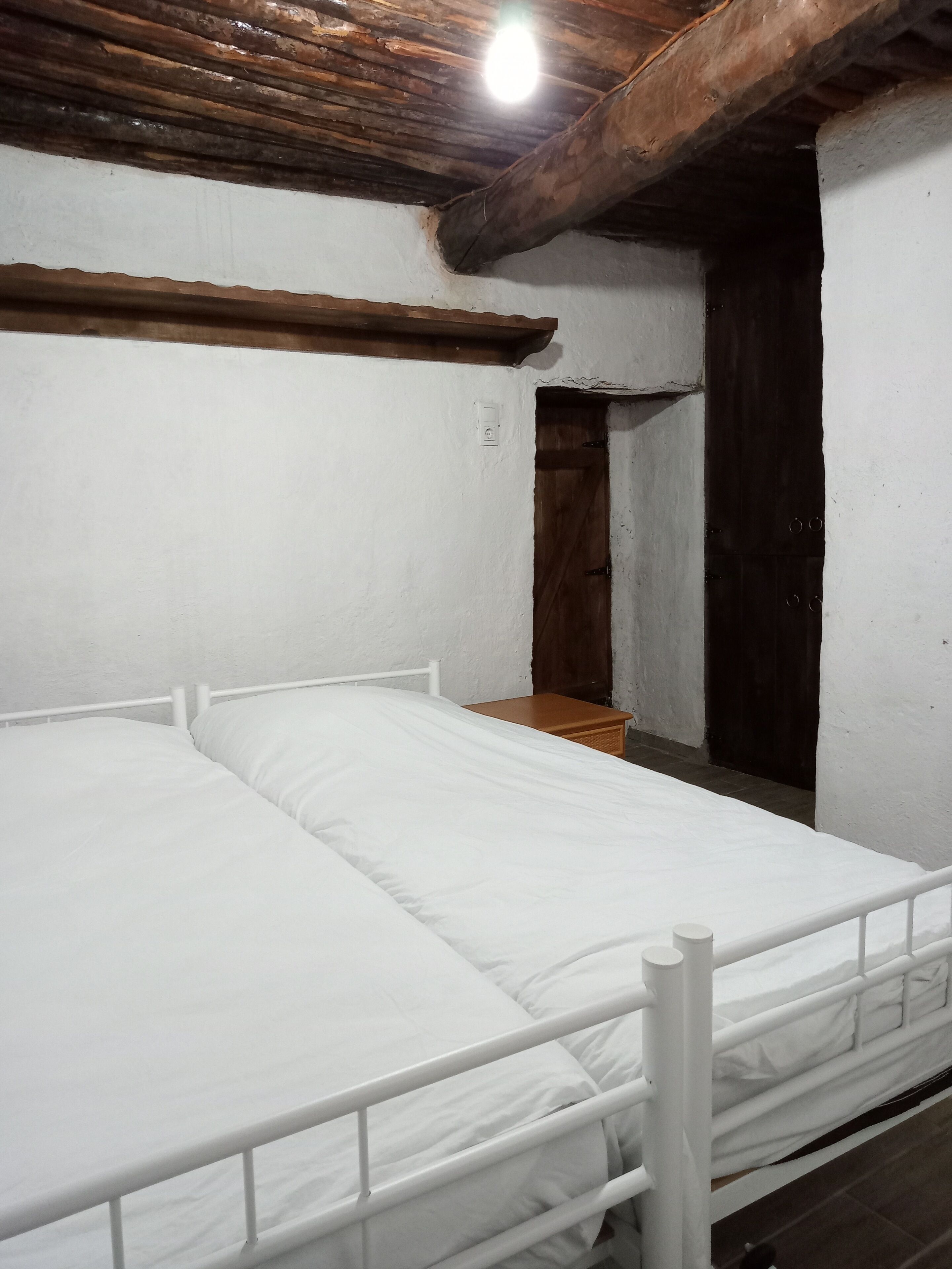 Quarto pequeno com uma cama de solteiro, roupa de cama branca, cabeceira de madeira e teto inclinado.