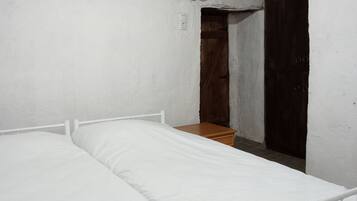 Quarto pequeno com uma cama de solteiro, roupa de cama branca, cabeceira de madeira e teto inclinado.