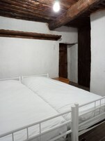 Quarto pequeno com uma cama de solteiro, roupa de cama branca, cabeceira de madeira e teto inclinado.