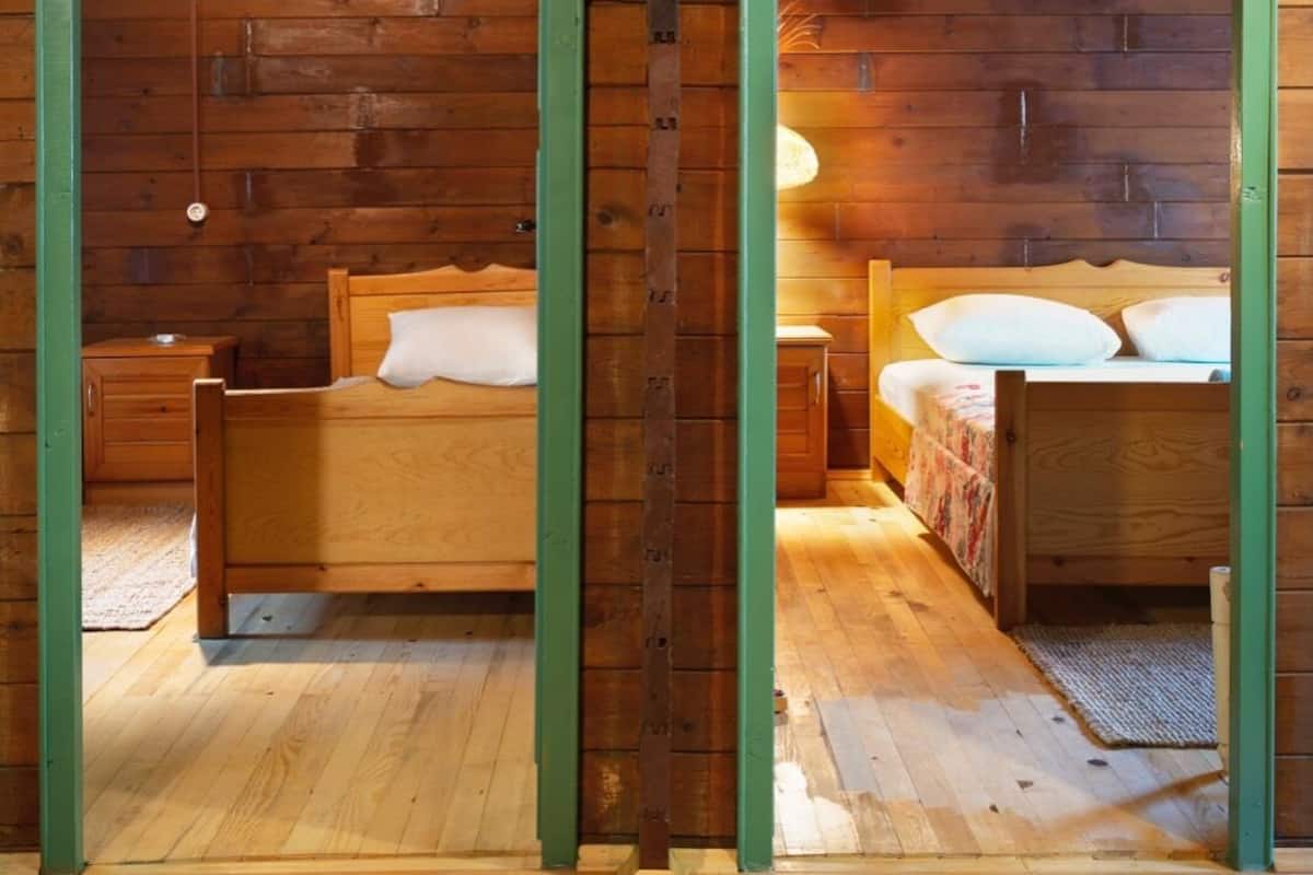 Uma cabana de madeira com duas camas de madeira, cada uma com estrutura verde, e um candeeiro pendente.