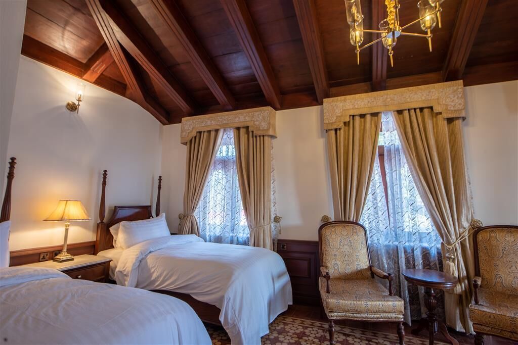 Quarto de hotel com duas camas, um candelabro e uma cadeira.