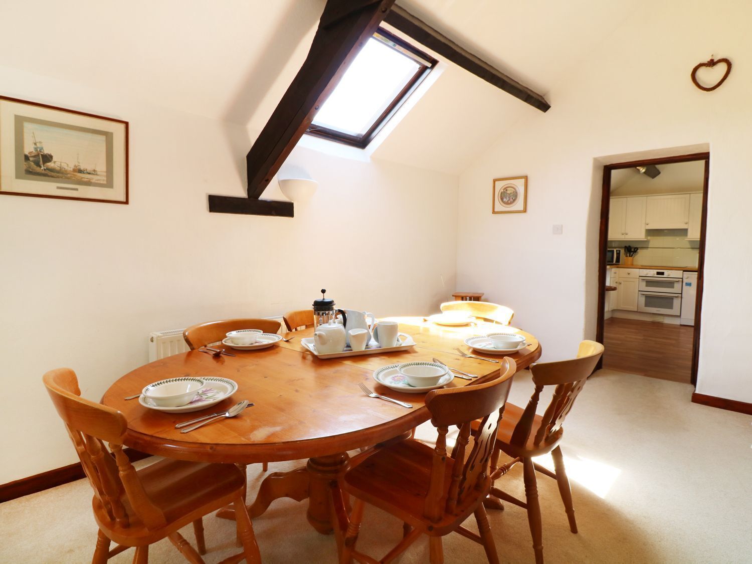 Uma sala de jantar com uma mesa de madeira redonda, seis cadeiras e um claraboia acima.
