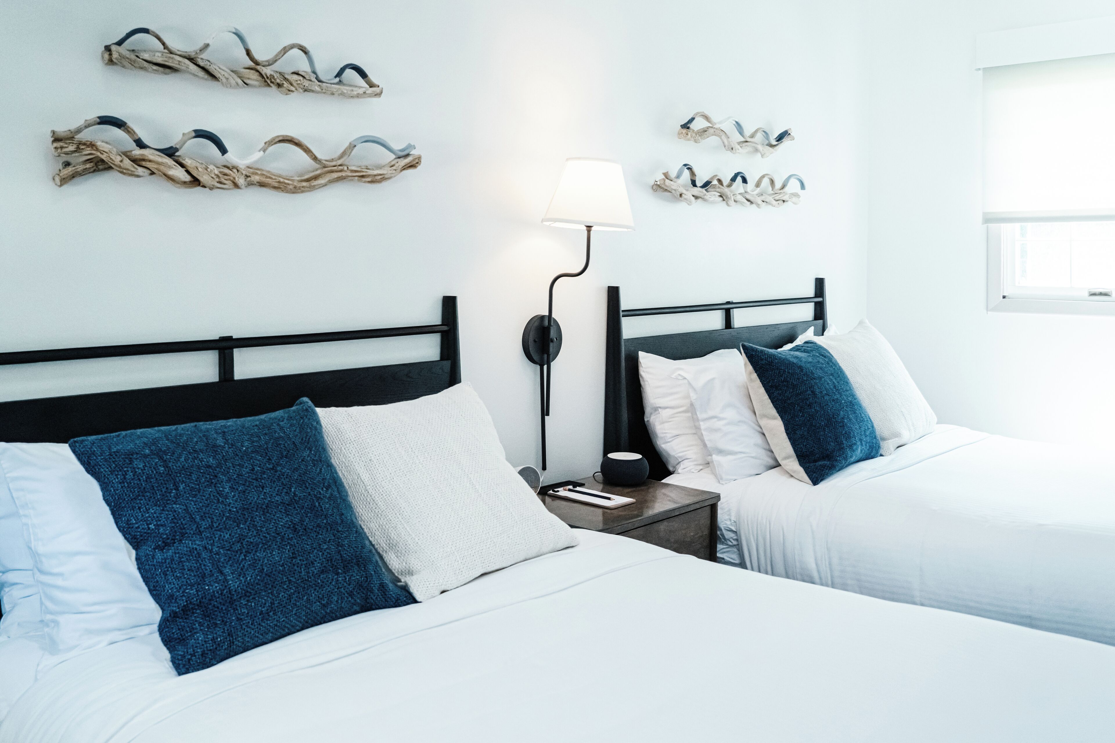 Quarto de hotel com duas camas, uma mesa de cabeceira, um abajur e decoração nas paredes.
