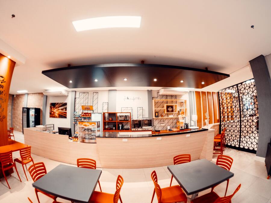 Um café moderno com balcão curvo, detalhes em madeira e cadeiras laranja.