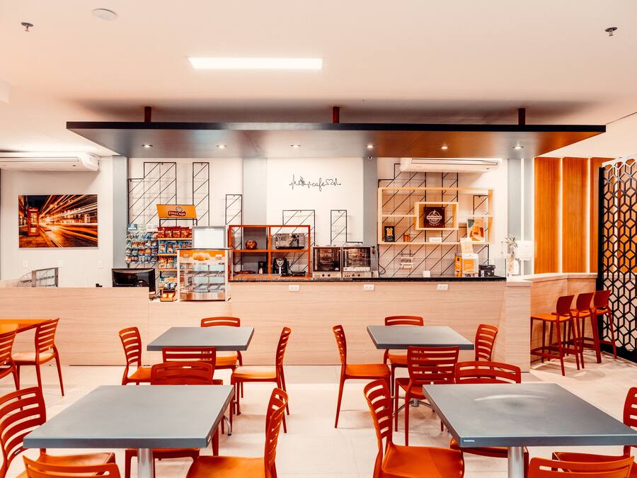Um café moderno com mesas e cadeiras, um balcão com menu e uma parede com padrão geométrico.