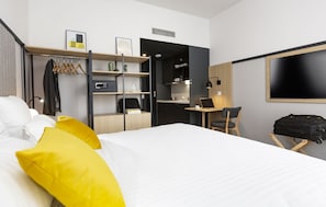 Quarto de hotel com cama, escrivaninha, cadeira, televisão e guarda-roupa.