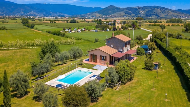 Uma casa com piscina, cercada por campos verdes e montanhas.