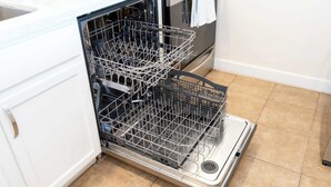 Uma máquina de lavar louça aberta com duas prateleiras e uma bandeja prateada.