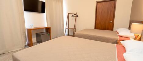 Quarto de hotel com duas camas, televisão presa na parede, escrivaninha de madeira e um guarda-roupa.