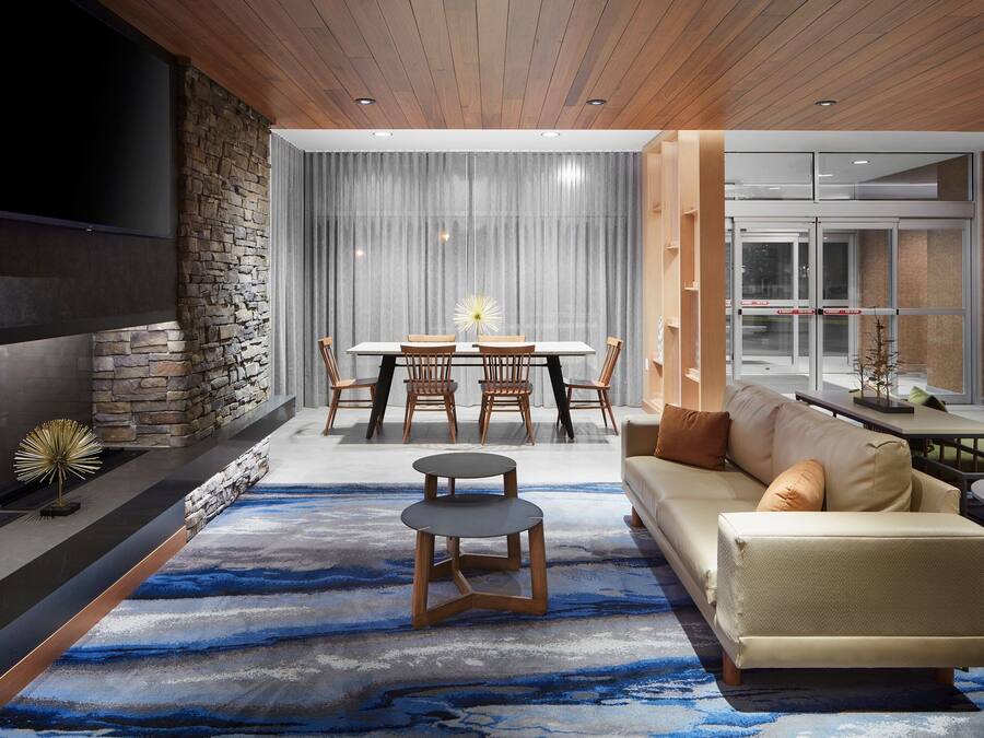 Uma sala de estar moderna com uma parede de destaque em pedra, uma TV de tela plana, uma área de jantar com mesa e cadeiras, e um sofá com almofadas.