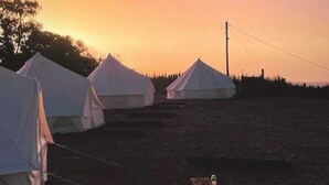 Uma fileira de tendas brancas em um camping, com o pôr do sol ao fundo.
