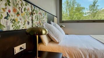 Quarto de hotel com cama, mesa de cabeceira, abajur e cabeceira estampada com flores.