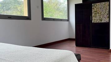 Quarto com cama, duas janelas, guarda-roupa e vista para árvores.