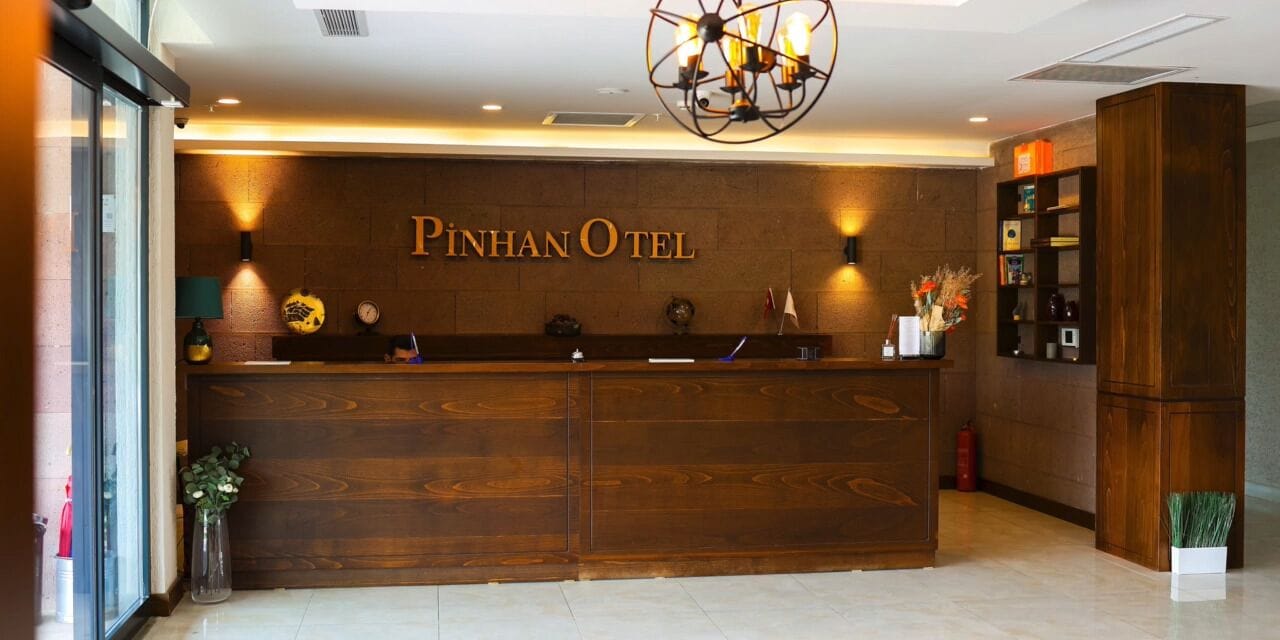 Uma receção com acabamento em madeira, um candelabro e um letreiro fixado na parede com a inscrição 'PINHAN OTEL'.