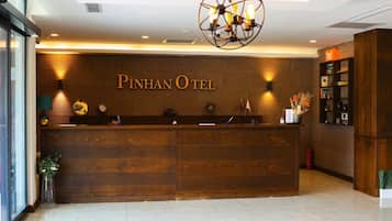 Uma receção com acabamento em madeira, um candelabro e um letreiro fixado na parede com a inscrição 'PINHAN OTEL'.