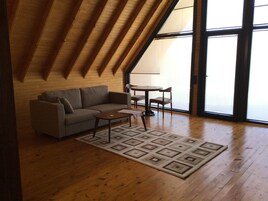 Um quarto de loft aconchegante com teto inclinado, um sofá cinza, uma mesa redonda pequena e um tapete estampado.