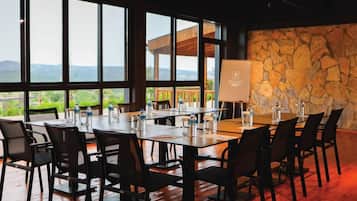 Uma sala de conferências com mesas, cadeiras, uma parede de pedra e vista para o exterior.