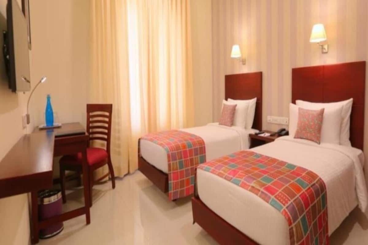 Quarto de hotel com duas camas, uma escrivaninha, uma cadeira e uma televisão.