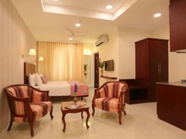 Quarto de hotel com uma cama, duas poltronas listradas, uma mesinha, televisão e guarda-roupa.