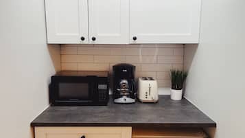 Uma cozinha com armários brancos, micro-ondas, máquina de café, torradeira e um vaso de planta.