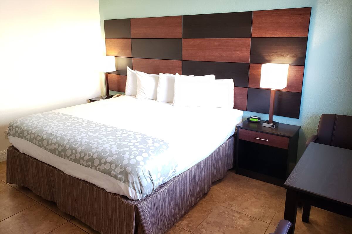 Quarto de hotel com uma cama grande, mesa de cabeceira com abajur, escrivaninha e uma cadeira.