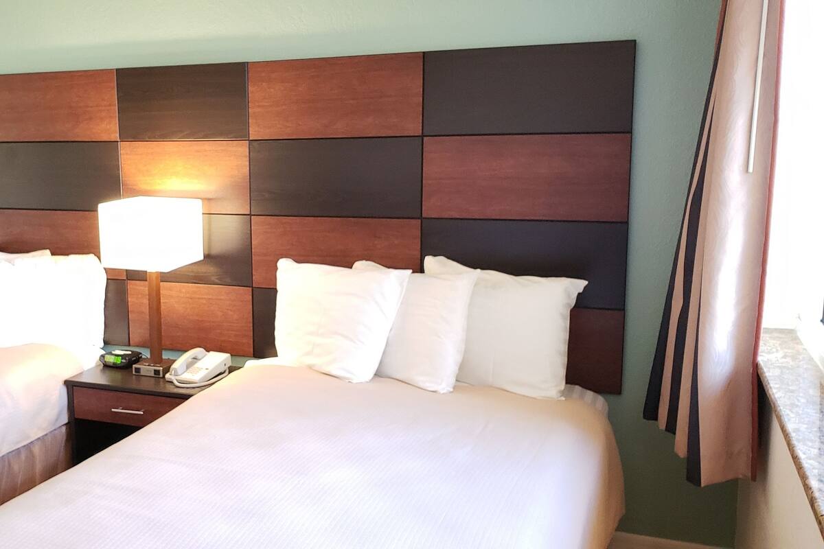 Quarto de hotel com duas camas, uma mesa de cabeceira com abajur e um telefone.