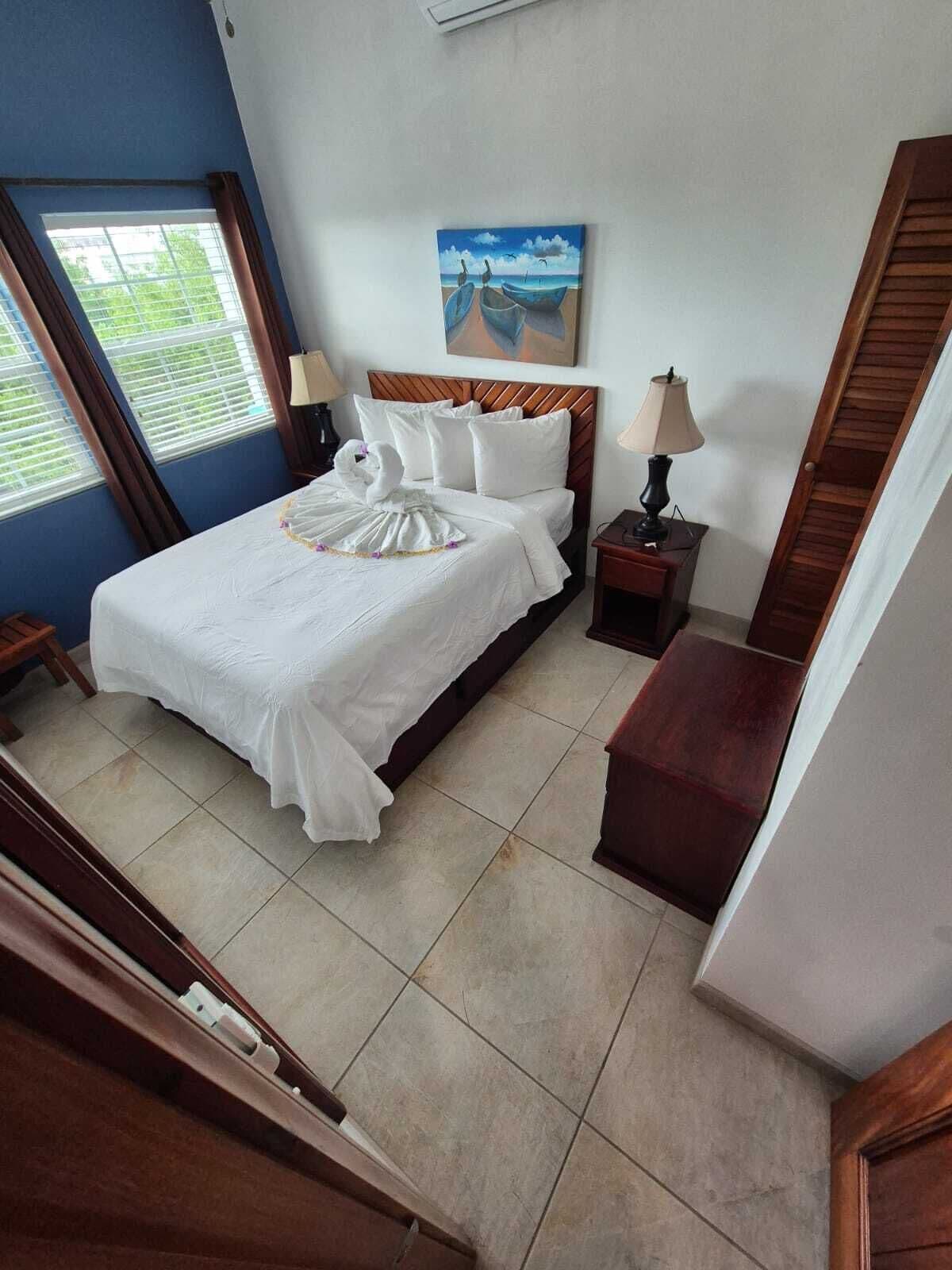 Quarto de hotel com cama, um quadro na parede, janela com cortinas e piso de madeira.