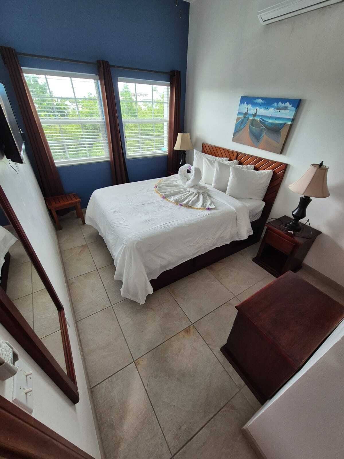 Quarto de hotel com uma cama, duas luminárias de cabeceira, um quadro na parede e uma janela com cortinas.