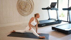 Mulher fazendo uma pose de yoga em um tapete em um quarto com uma esteira e uma decoração circular fixada na parede.