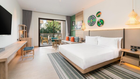Quarto de hotel moderno com uma cama grande, uma escrivaninha, uma cadeira, varanda com mobiliário exterior e obras de arte nas paredes.