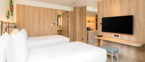 Quarto de hotel com duas camas, televisão, um espaço de estar pequeno e uma cozinha compacta.