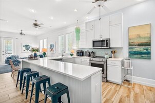 Uma cozinha moderna com armários brancos, uma ilha central com banquetas, micro-ondas e um quadro grande na parede.