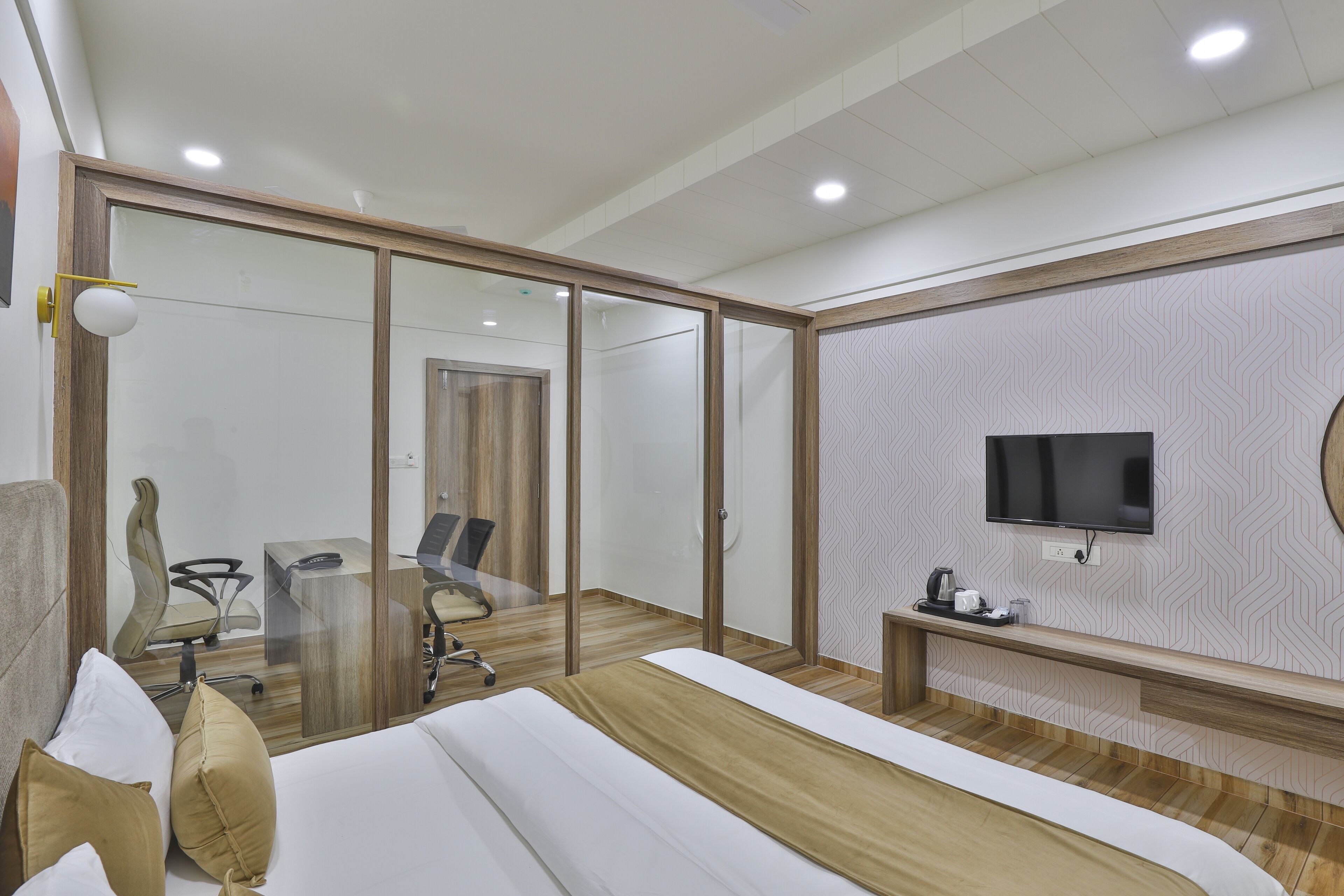 Quarto de hotel moderno com uma cama grande, uma escrivaninha com cadeira, uma televisão na parede e um espelho.