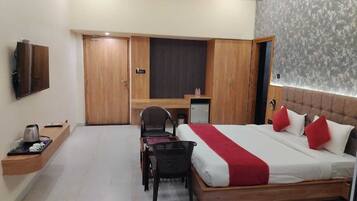 Quarto de hotel com cama, escrivaninha, cadeira, televisão e guarda-roupa.