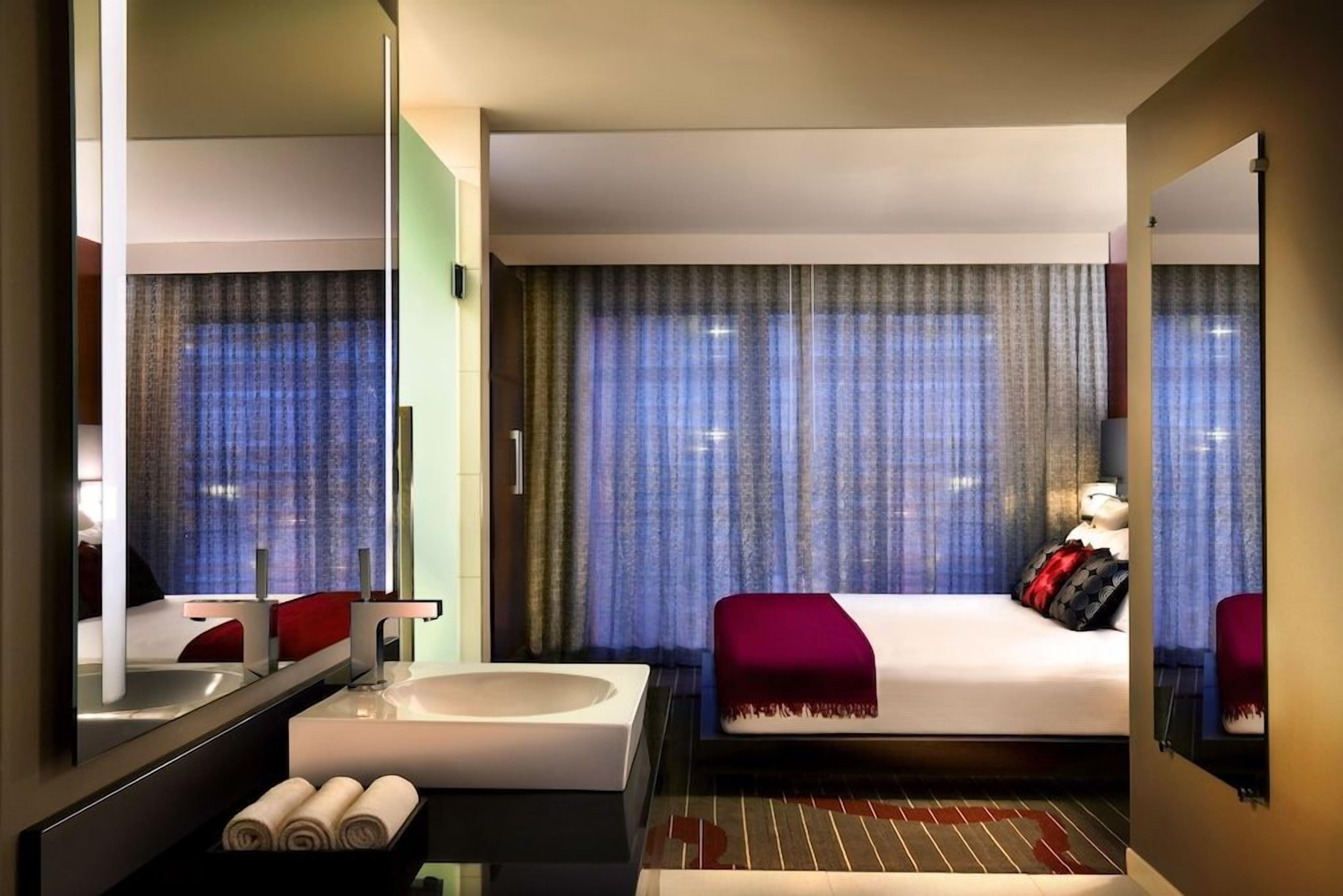 Quarto de hotel com uma cama grande, banheiro com banheira e um espelho amplo.