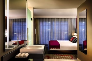 Quarto de hotel com uma cama grande, banheiro com banheira e um espelho amplo.