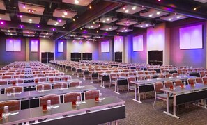 Uma sala de conferências com fileiras de mesas e cadeiras, equipada com placas de identificação e copos de água.