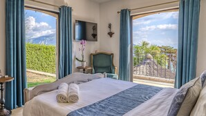 Quarto de hotel com uma cama grande, uma cadeira, uma mesa pequena e uma televisão na parede.