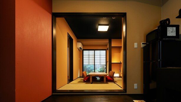 Um quarto japonês tradicional com tatames, uma mesa baixa com almofadas e uma porta deslizante que dá para uma área verde.