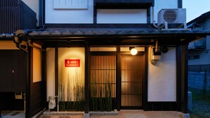 Um edifício japonês tradicional com porta deslizante, pequena área de entrada com degraus e uma placa.