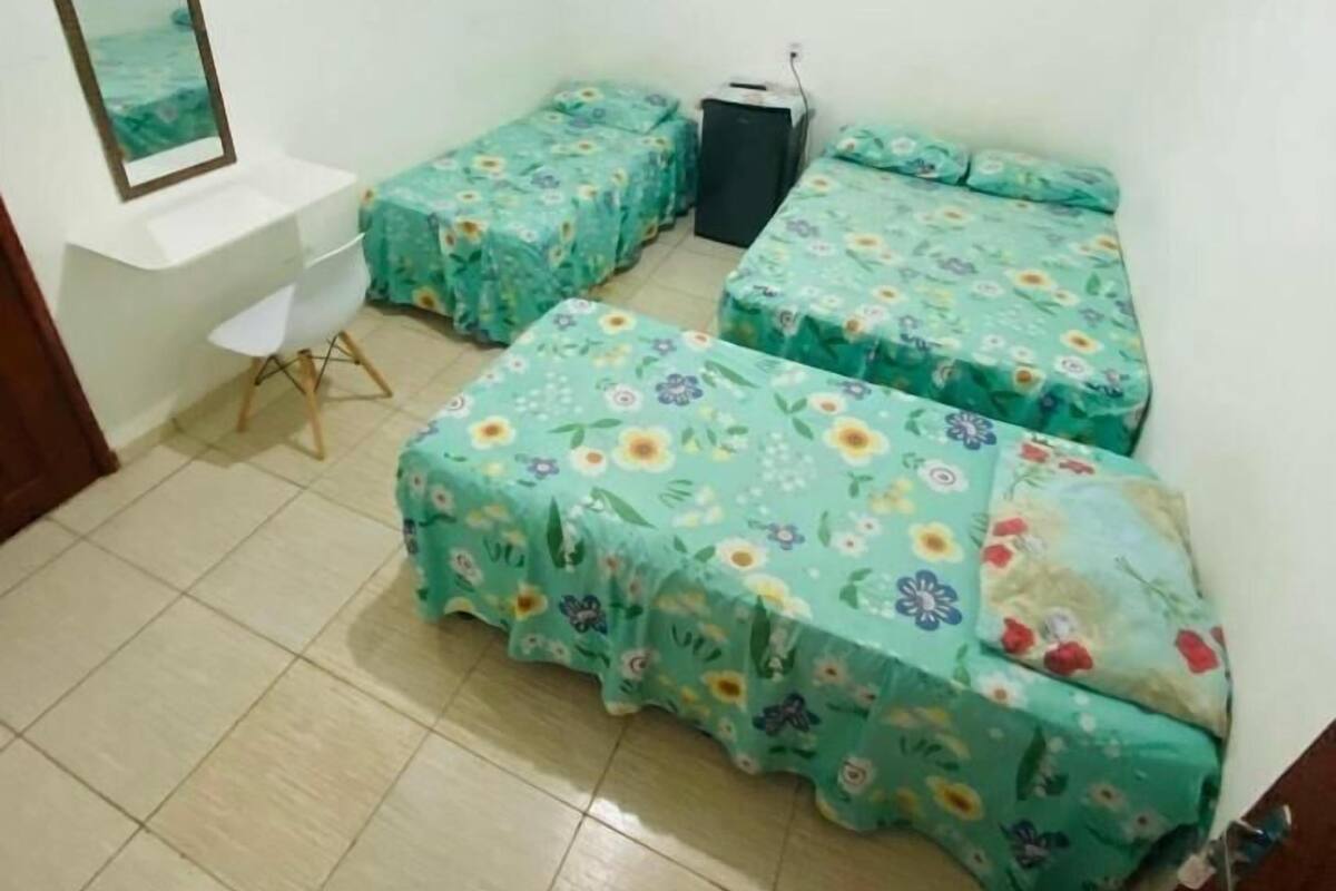 Quarto pequeno e limpo, com uma cama, uma escrivaninha e um espelho.
