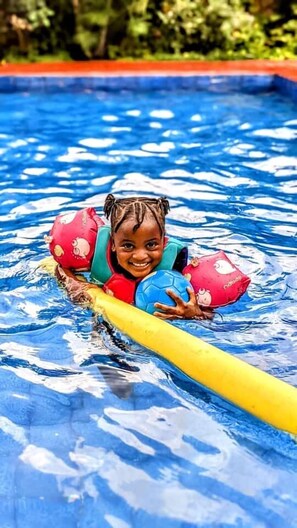 Uma criança em uma piscina com um flutuador amarelo e coletes salva-vidas vermelhos.