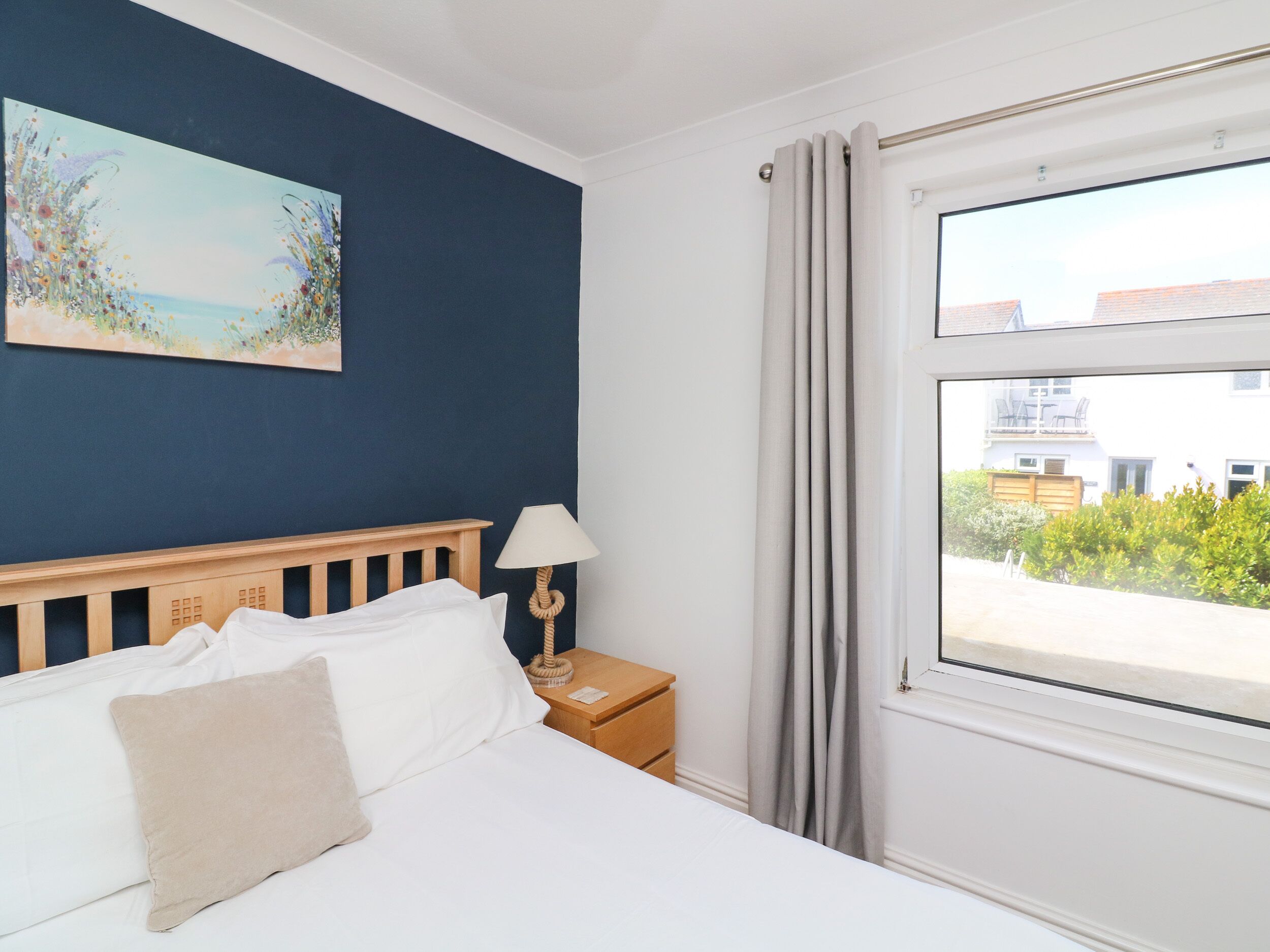 Quarto de hotel com uma cama, mesa de cabeceira com abajur, um quadro na parede e janela com cortinas.