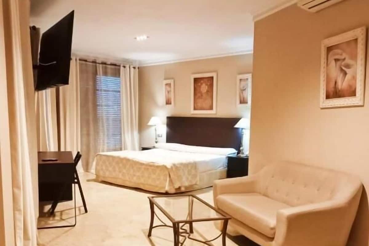 Quarto de hotel com cama, sofá, televisão e pequena mesa.