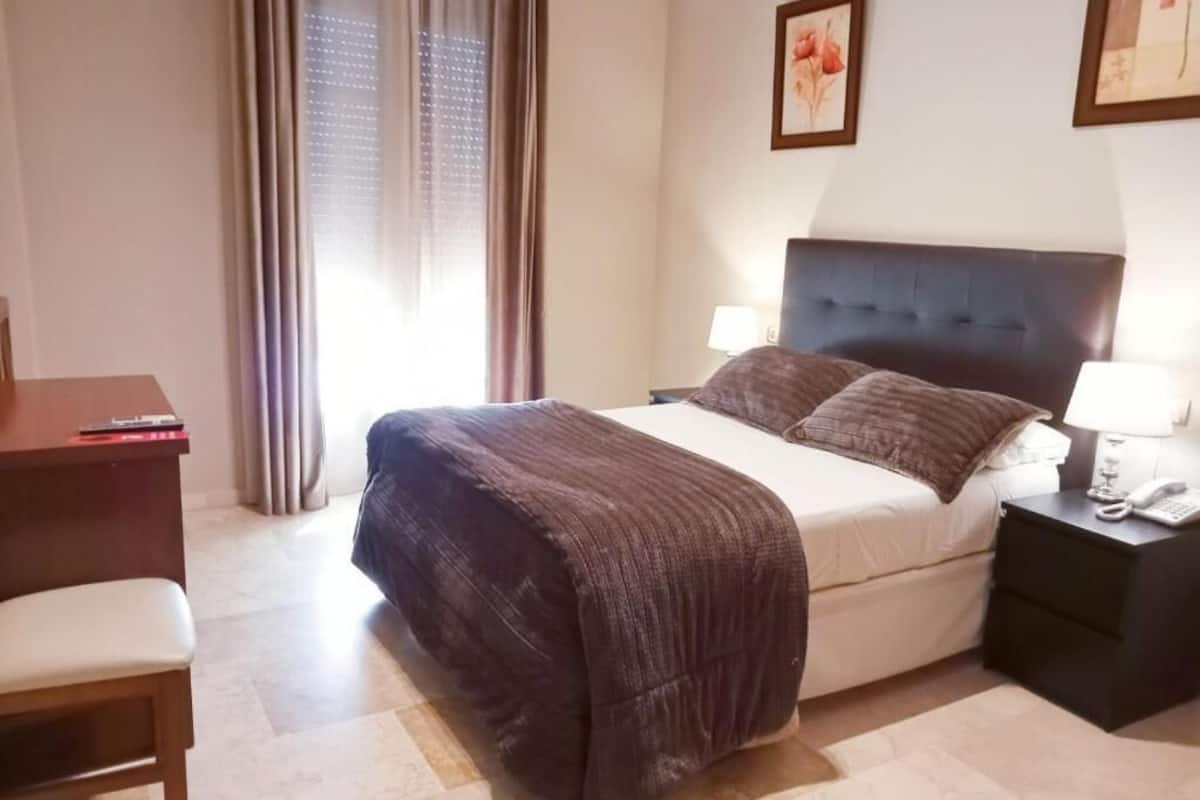 Quarto de hotel com cama, mesas de cabeceira, escrivaninha e uma cadeira.