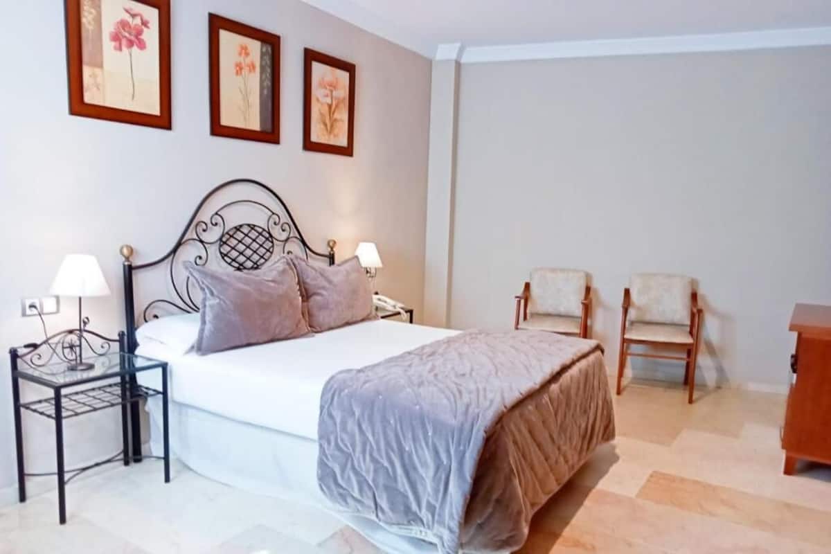 Quarto com cama, mesas de cabeceira, uma cadeira e cômoda.