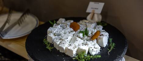 Uma travessa de ardósia preta com cubos de queijo branco, adornada com ervas e nozes, sobre um bordado de renda.